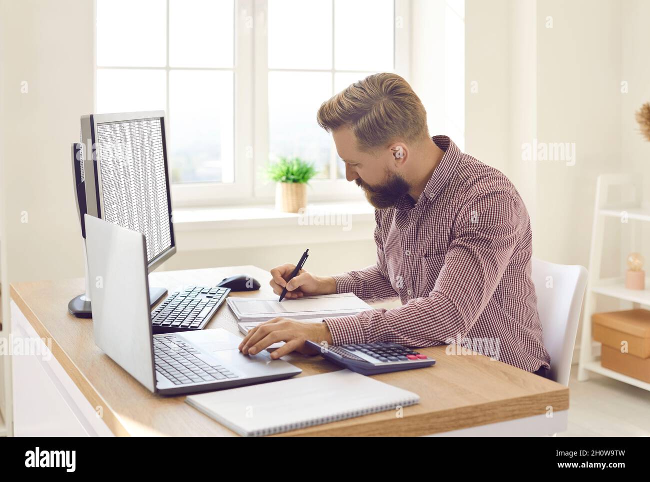 Financial accountant writing something down while working on computers ...