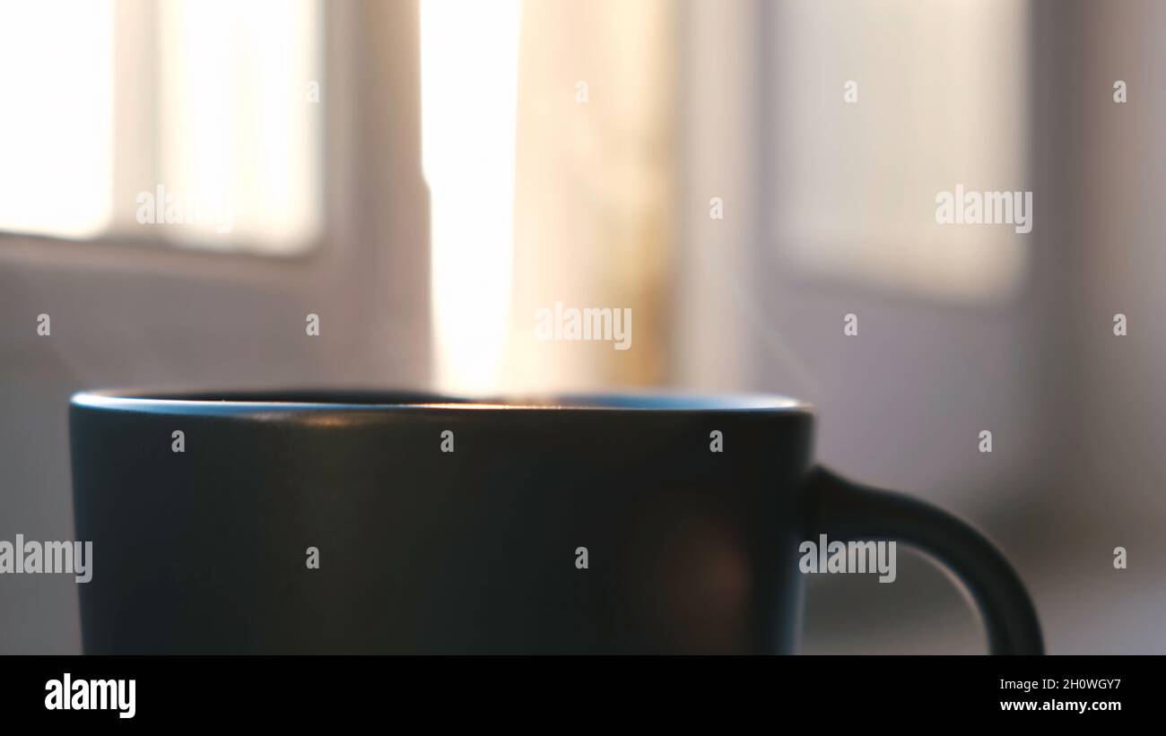 Coffee or tea mug on a window sill. Close up of the hot beverage in the ...