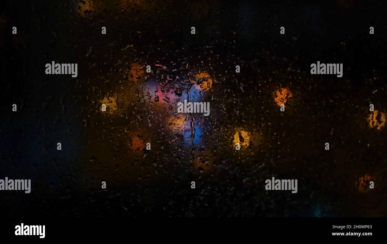 Close-up of raindrops on glass on background of blurred lights in dark ...