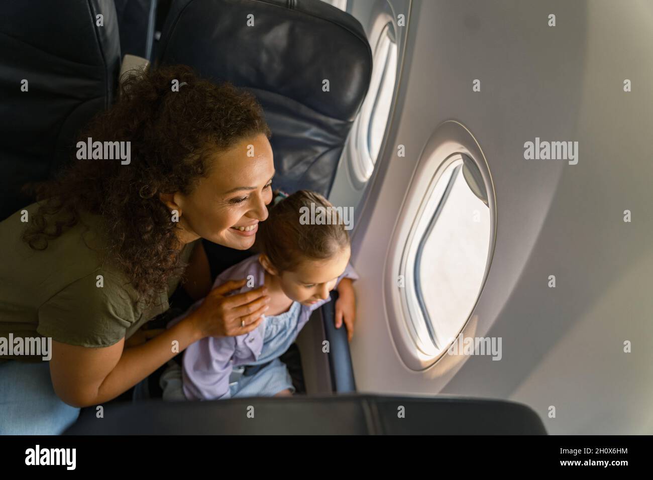 Smiling mom and her kid looking at the scenery outside the plane window ...