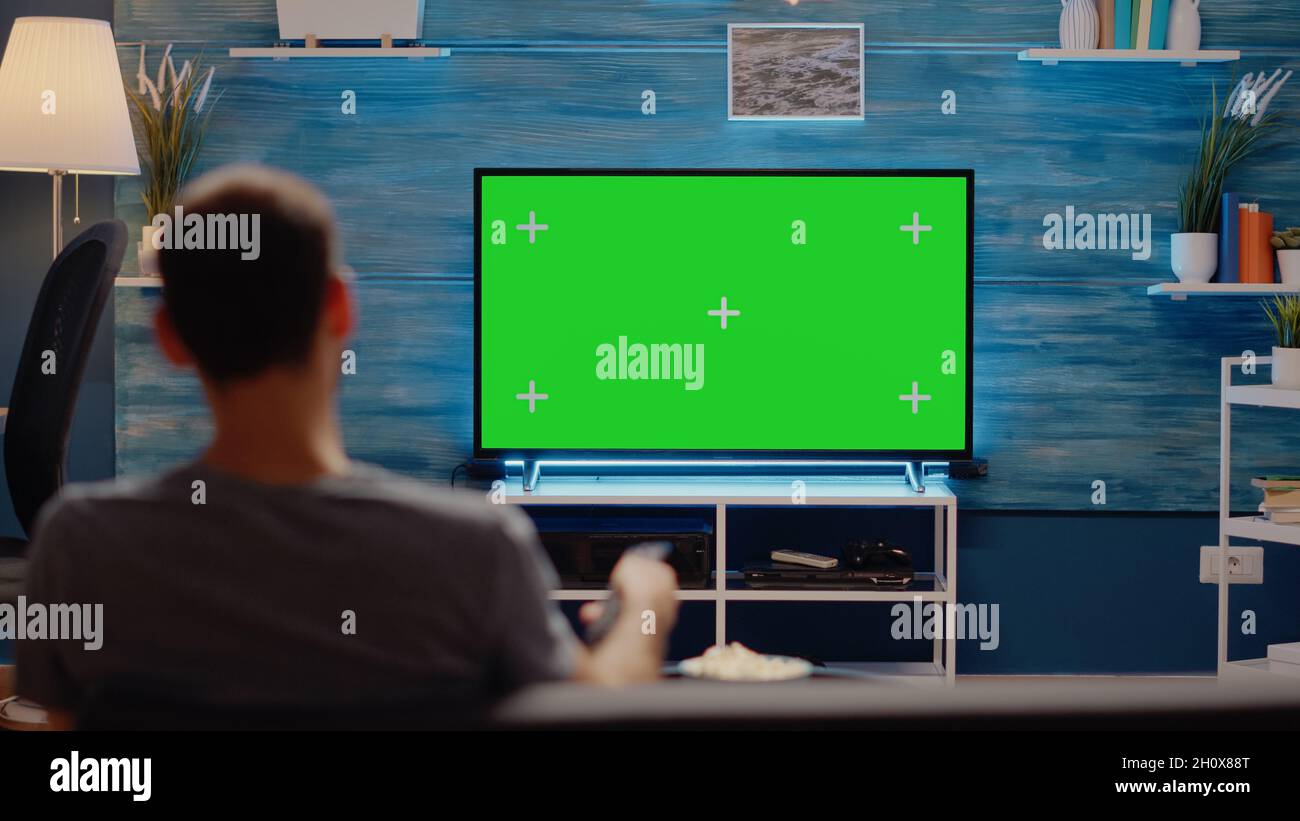 Man using TV remote on green screen background at home. Mockup template ...