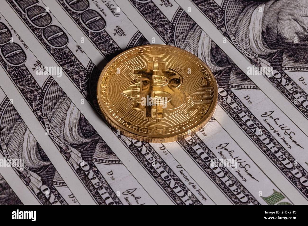 Gold bitcoin on one hundred dollar bills. The coin reflects the eyes of ...