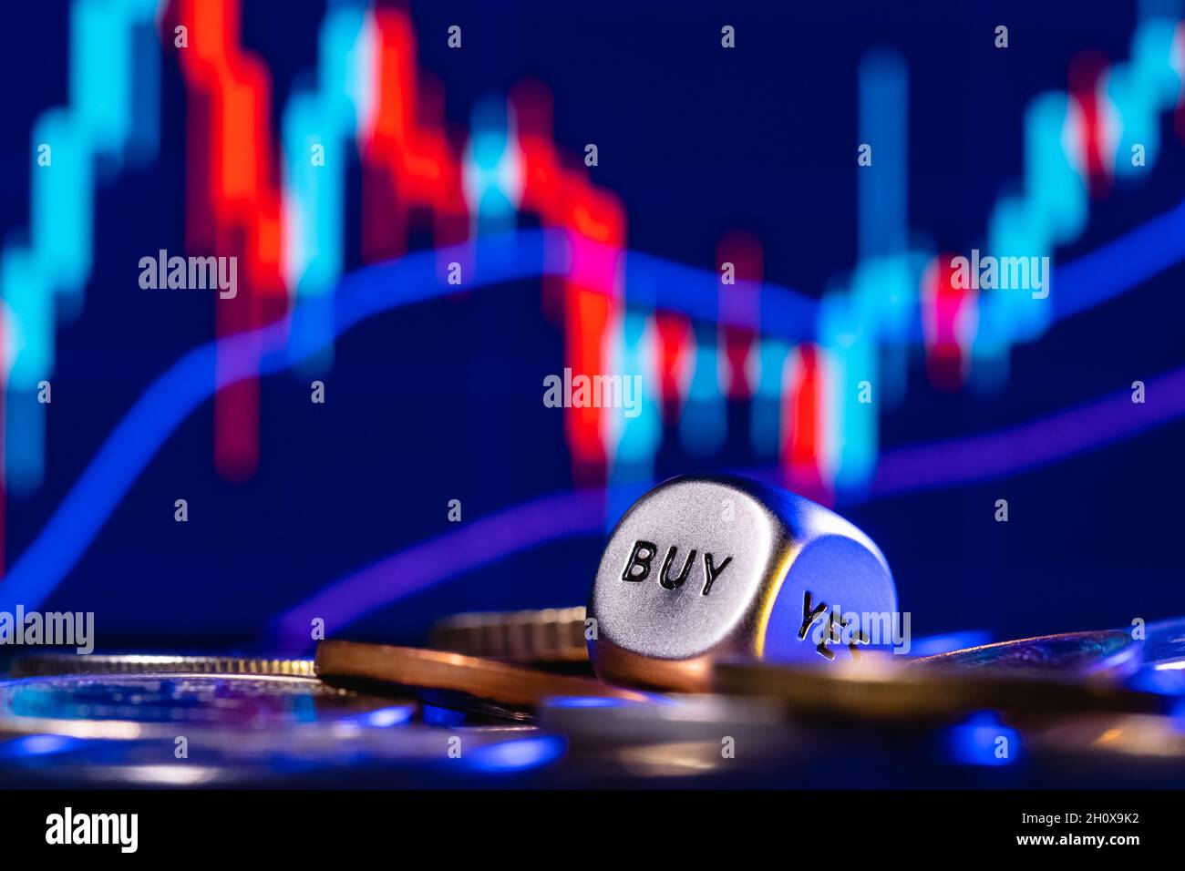 A metal dice in a pile of coins. On the background the stock chart with ...