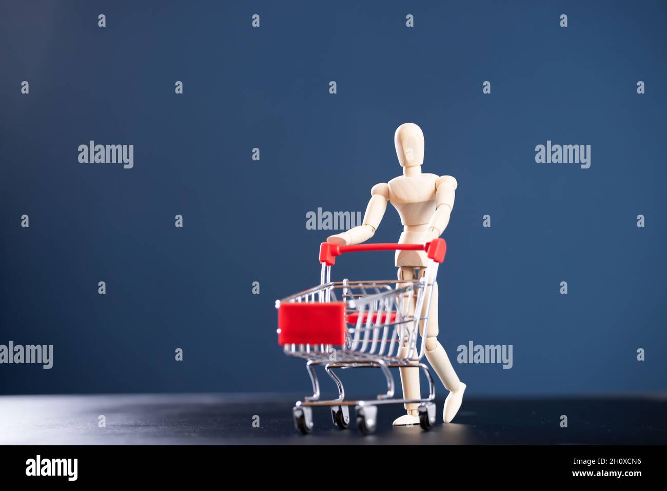 Go shopping concept. Wooden figure with shopping cart on blue ...