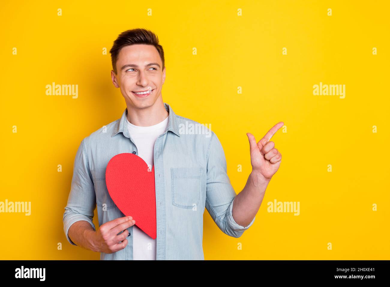 Portrait of attractive cheerful guy hiding heart showing copy space ad ...