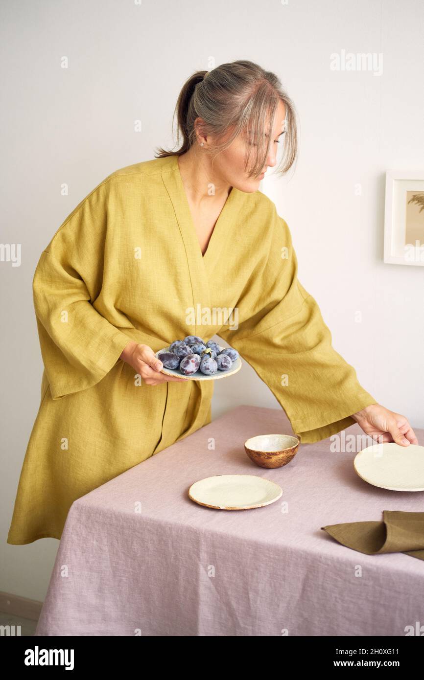 Young girl in a dressing gown lays the table. Natural fabrics and ...
