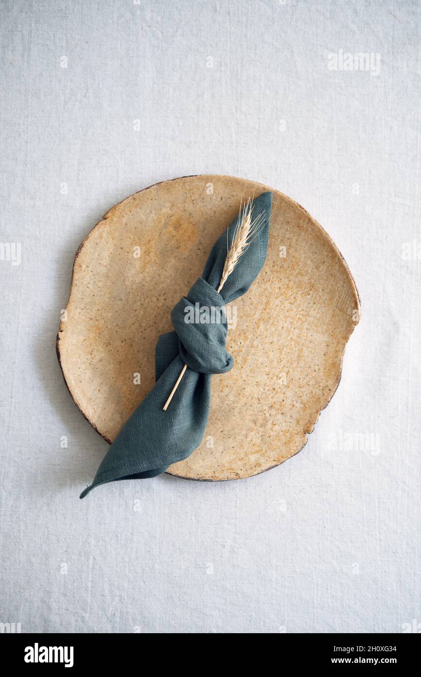 Table setting with empty brown plate and grey linen napkin tied in a ...