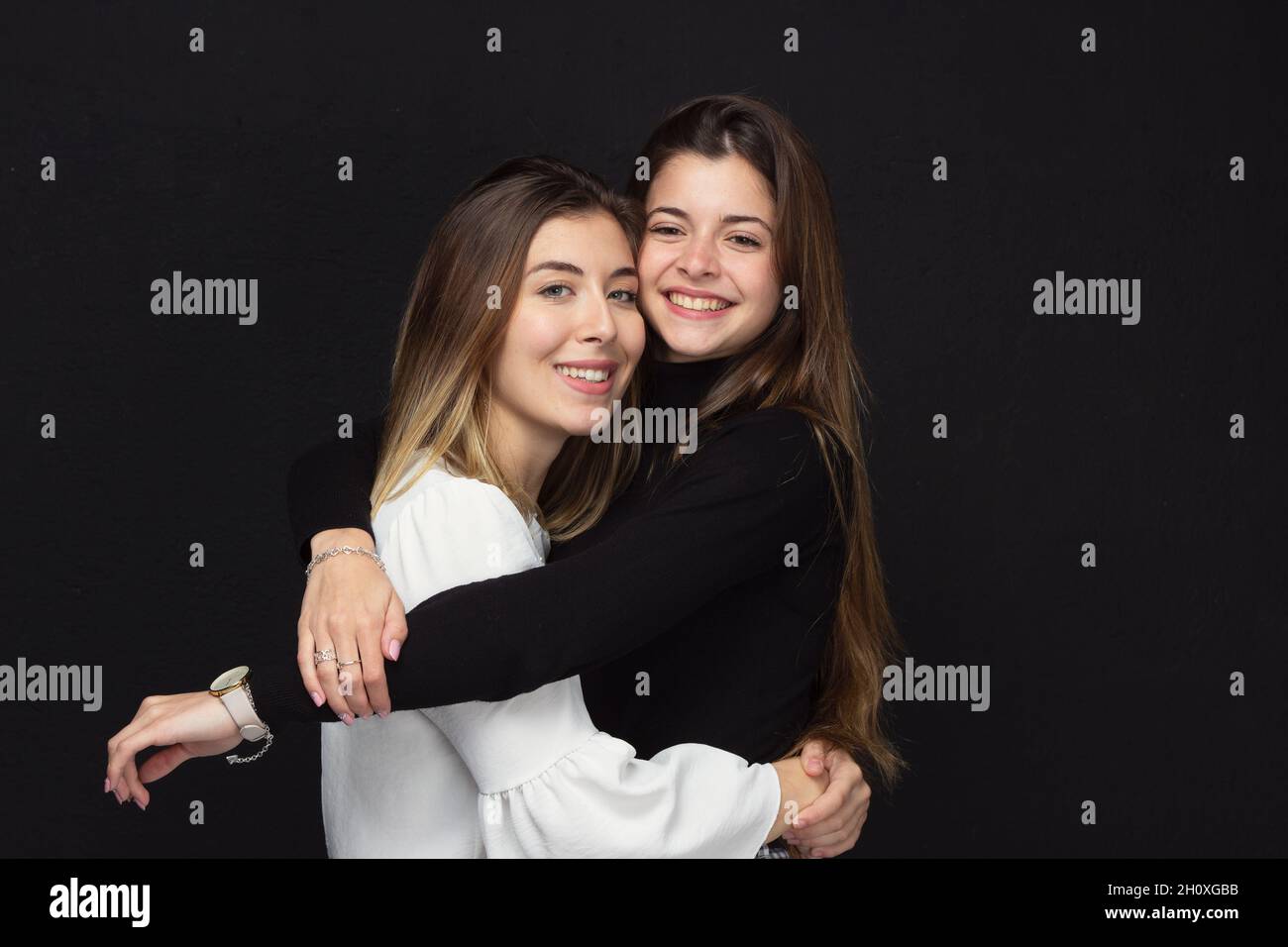 Two beautiful friends embrace looking at the camera on a black ...