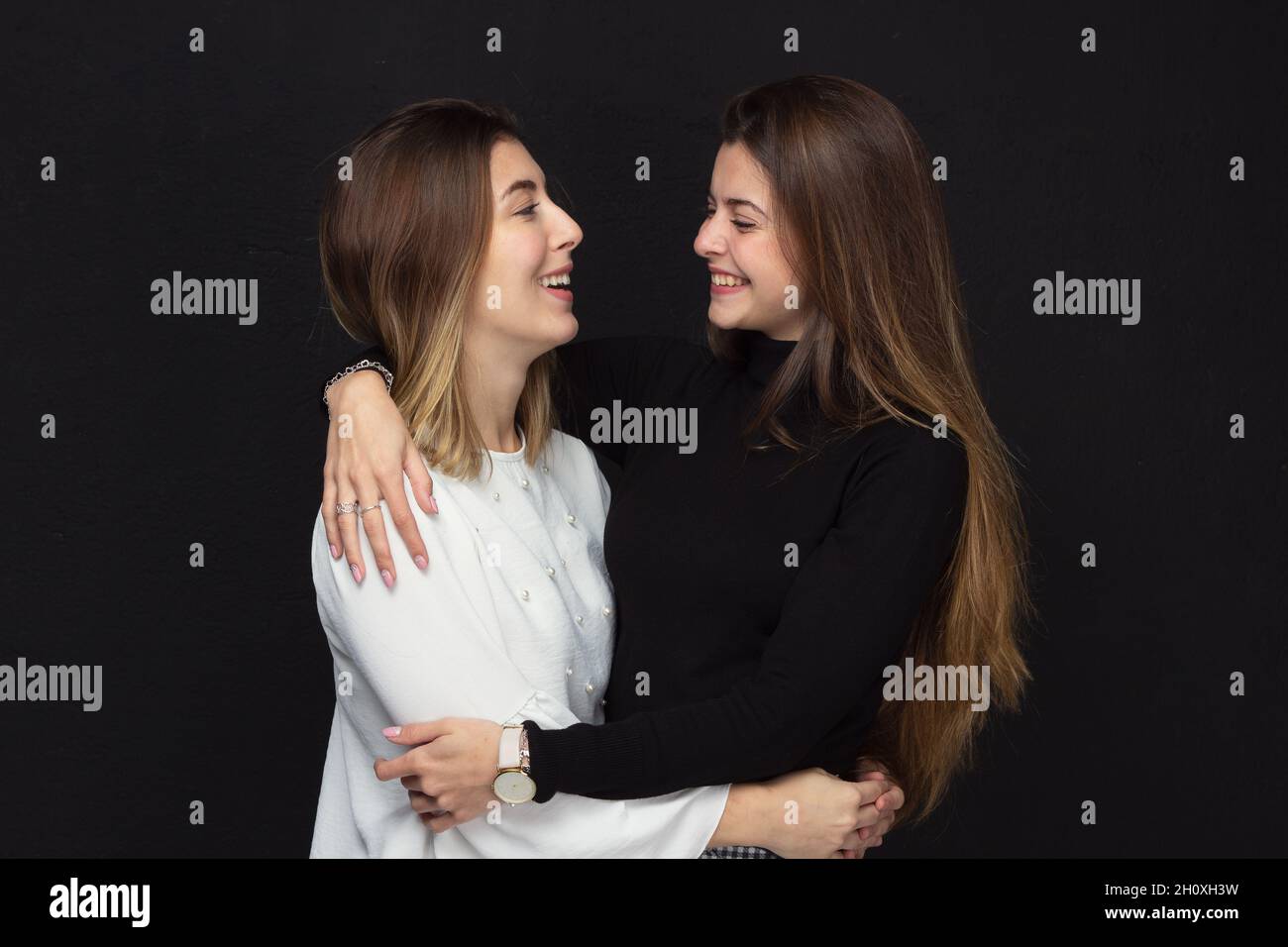 Two beautiful friends embrace while looking at each other on black ...