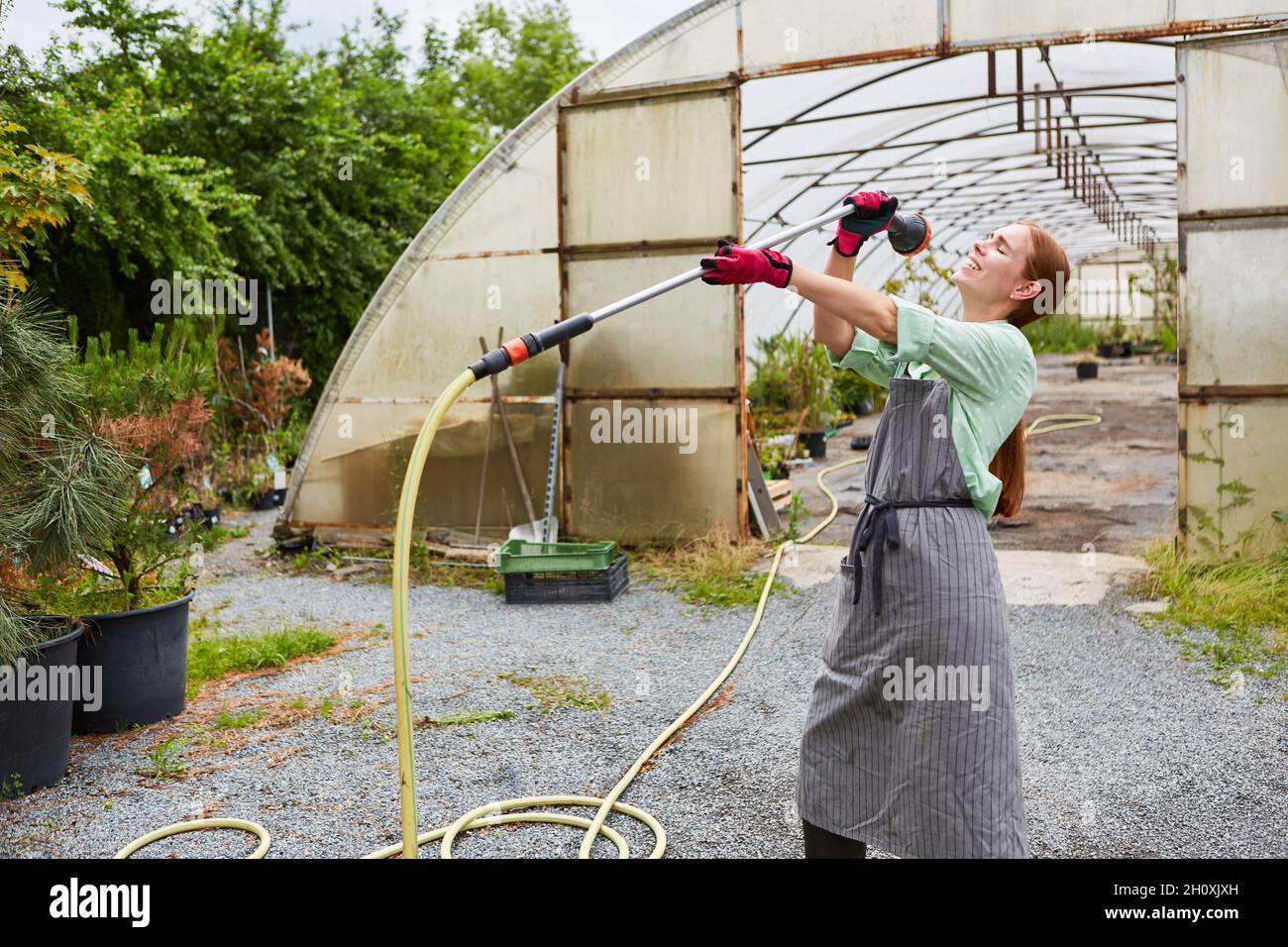 Young woman as a gardener apprentice has fun and sings for joy into a ...