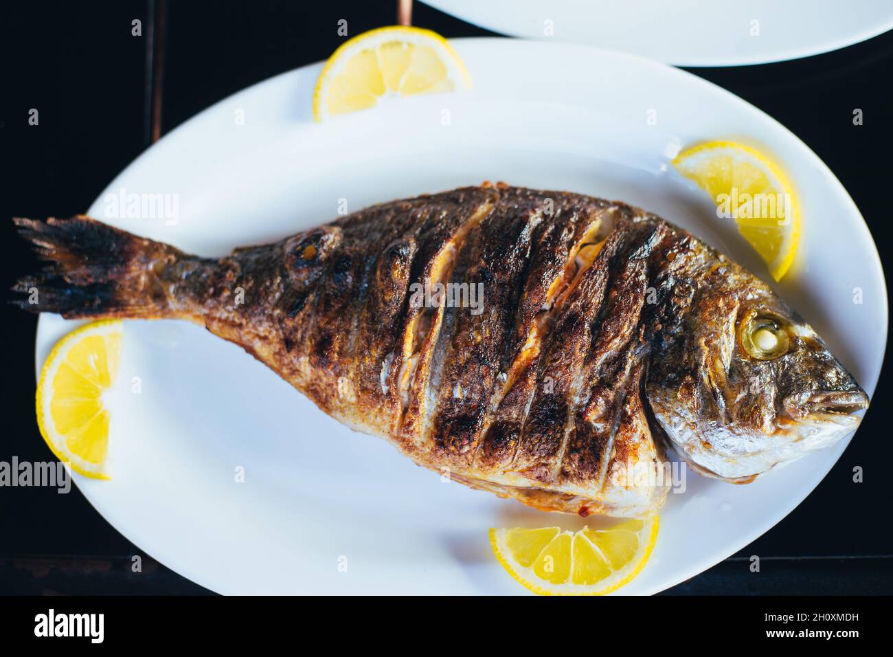 Fried fish with lemon wedges on a white plate - sea bass and dorado ...