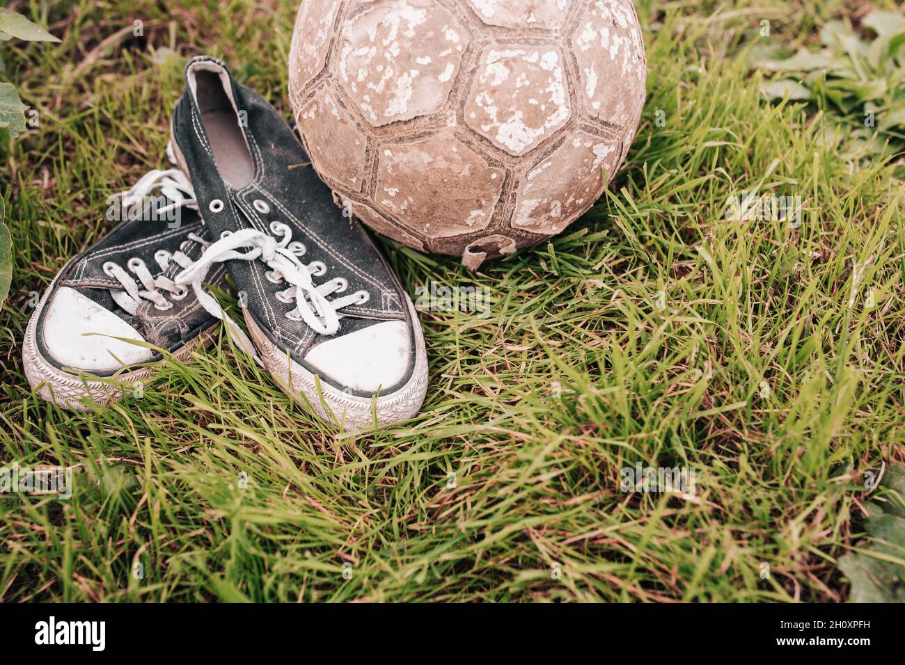 Old sports sneakers and a torn leather ball - worn out items and ...
