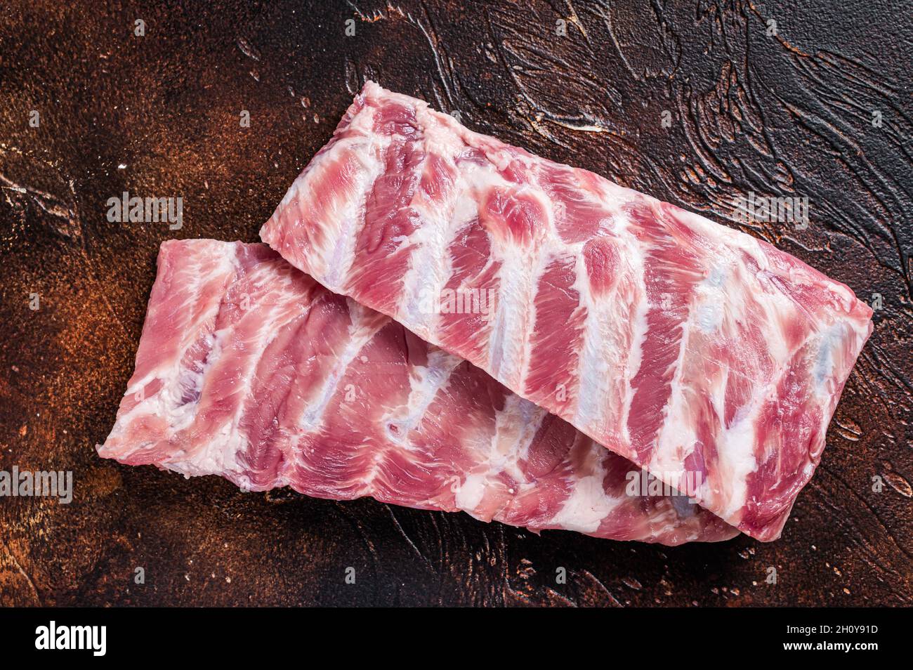 Rack of raw pork spare ribs on butcher table. Dark background. Top view ...