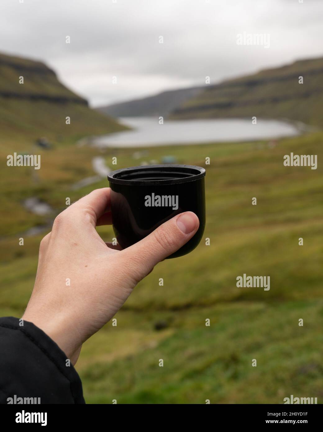 Vertical shot of a hand with a cup with liquid on nature background in ...