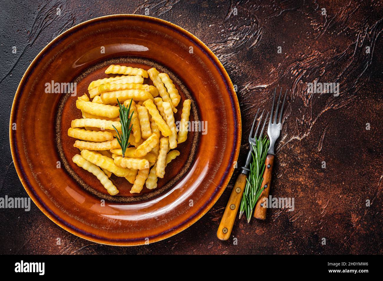 Fried Crinkle French fries potatoes or chips in a rustic plate. Dark ...