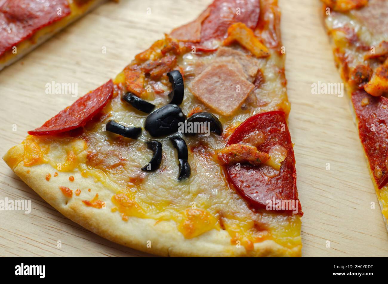 Meat feast pizza on thin dough decorated with black olives in the shape ...