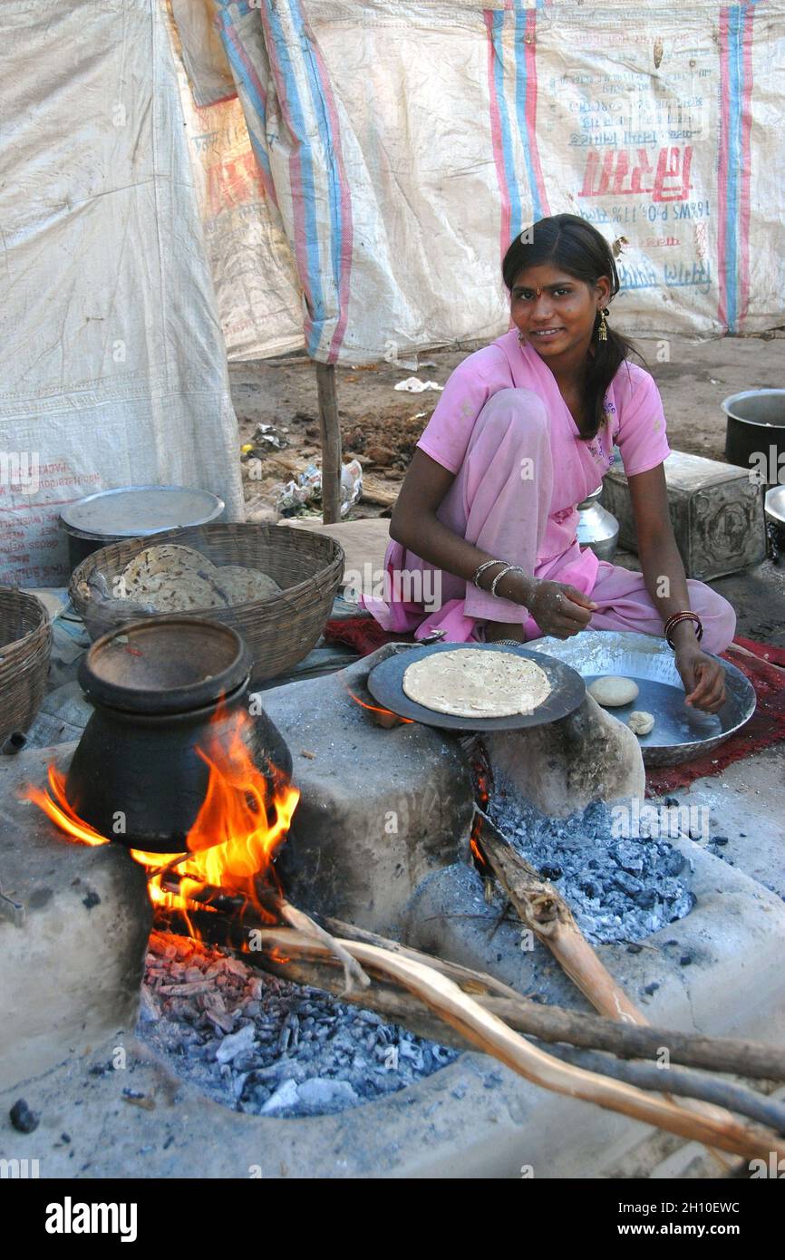 A young girl making chappatis and roti on an open fire using fire wood ...