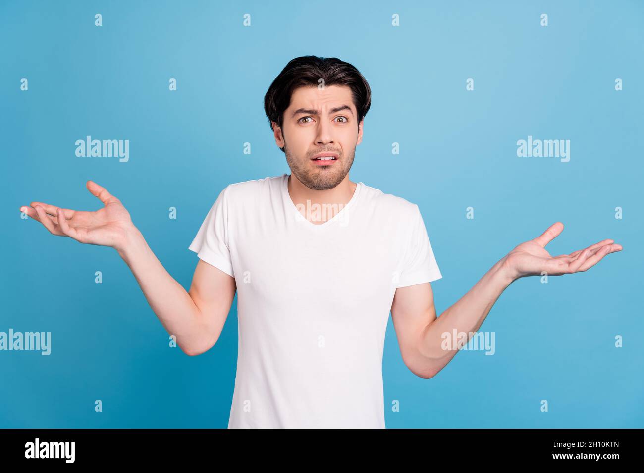 Photo of unsure troubled guy shrug shoulders confused face wear white t-shirt isolated blue ...