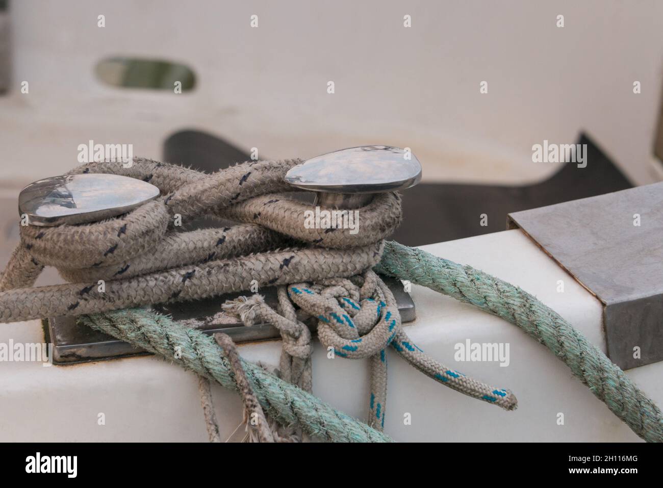 Ship bollard with green and grey ropes to which a blue boat is moored ...