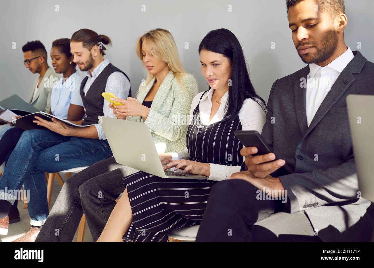 Multiracial people using laptops and cellphones while waiting in line ...