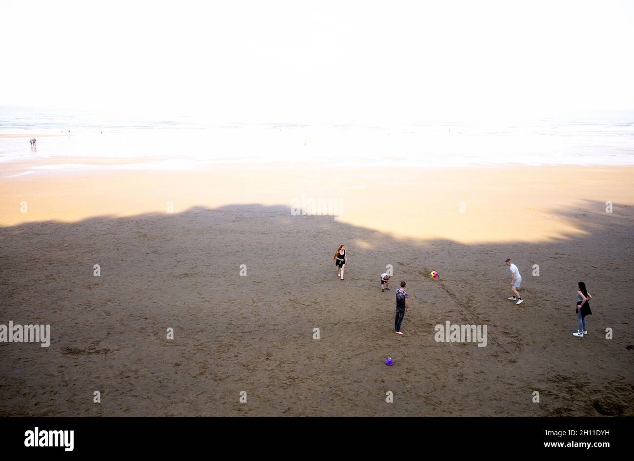 Bleached out sea at Scarborough while a family play ball in the shadow ...