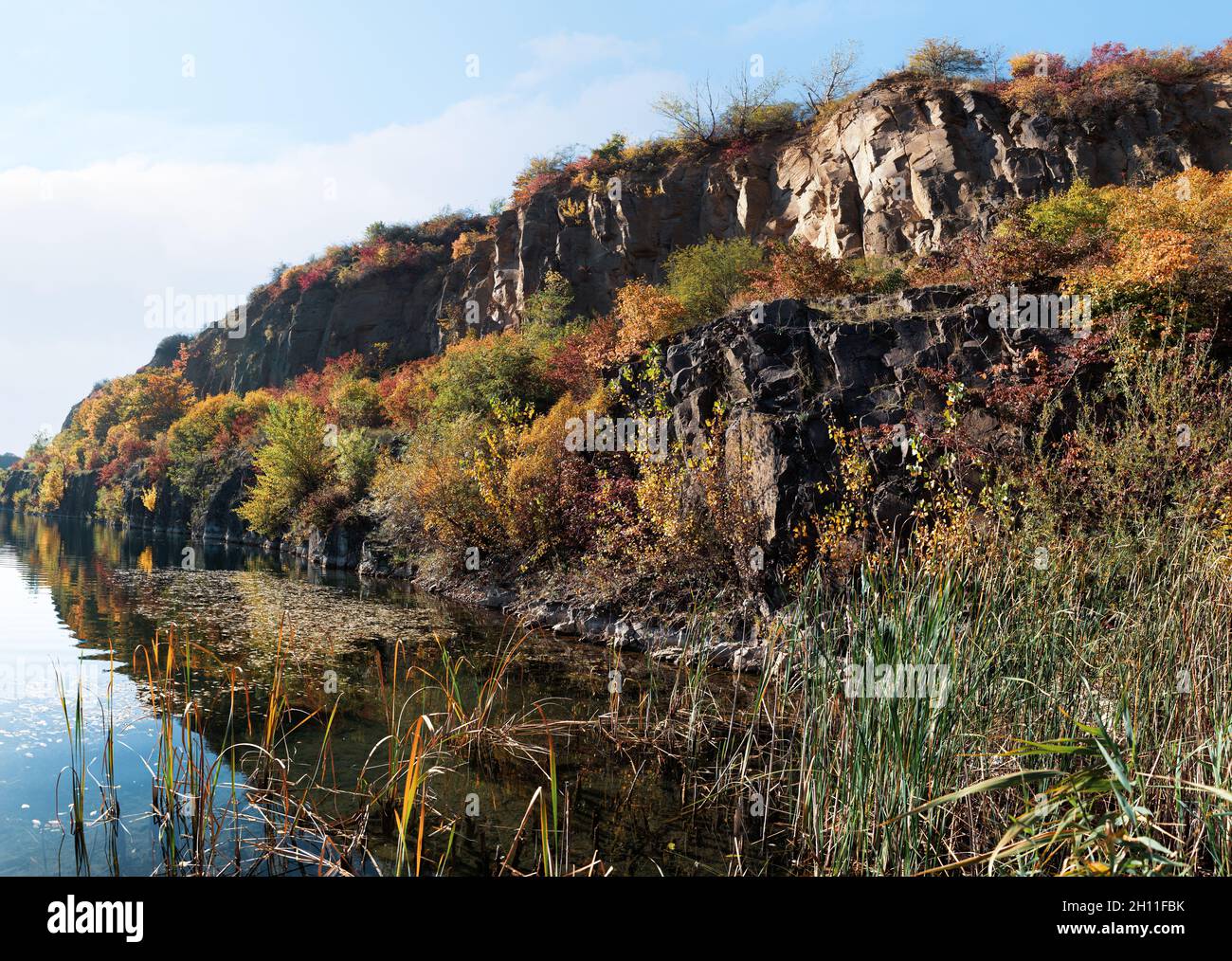 Golden autumn with colourful trees in old flooded quarry. Rocks, lake ...