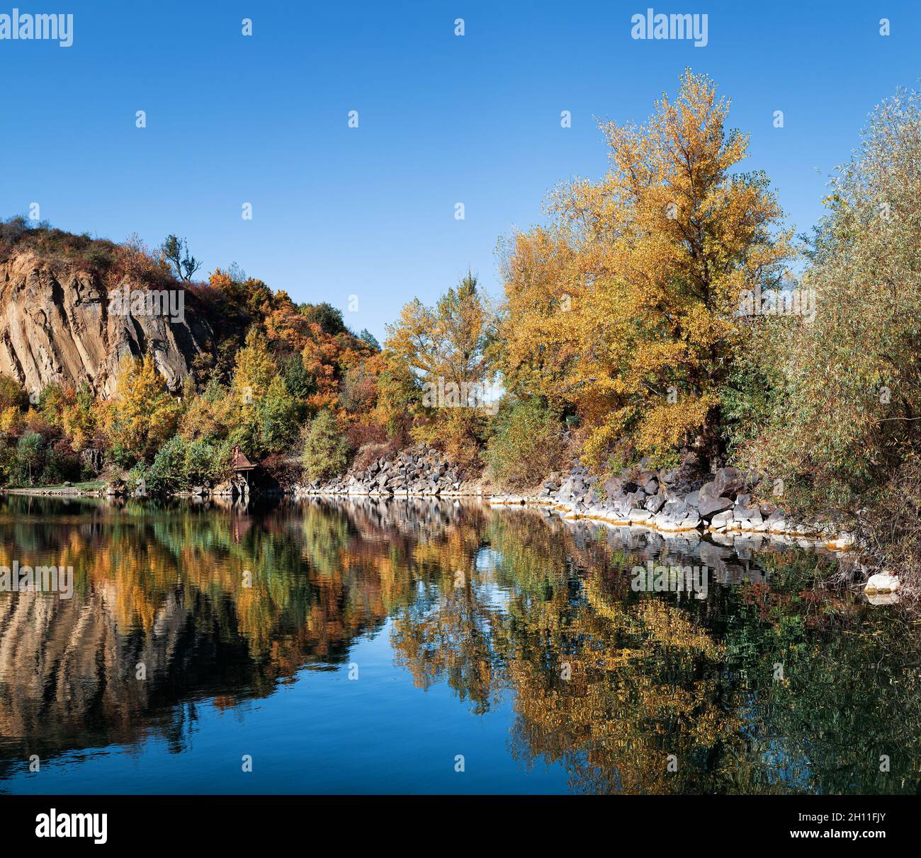 Golden autumn with colourful trees in old flooded quarry. Rocks, lake ...