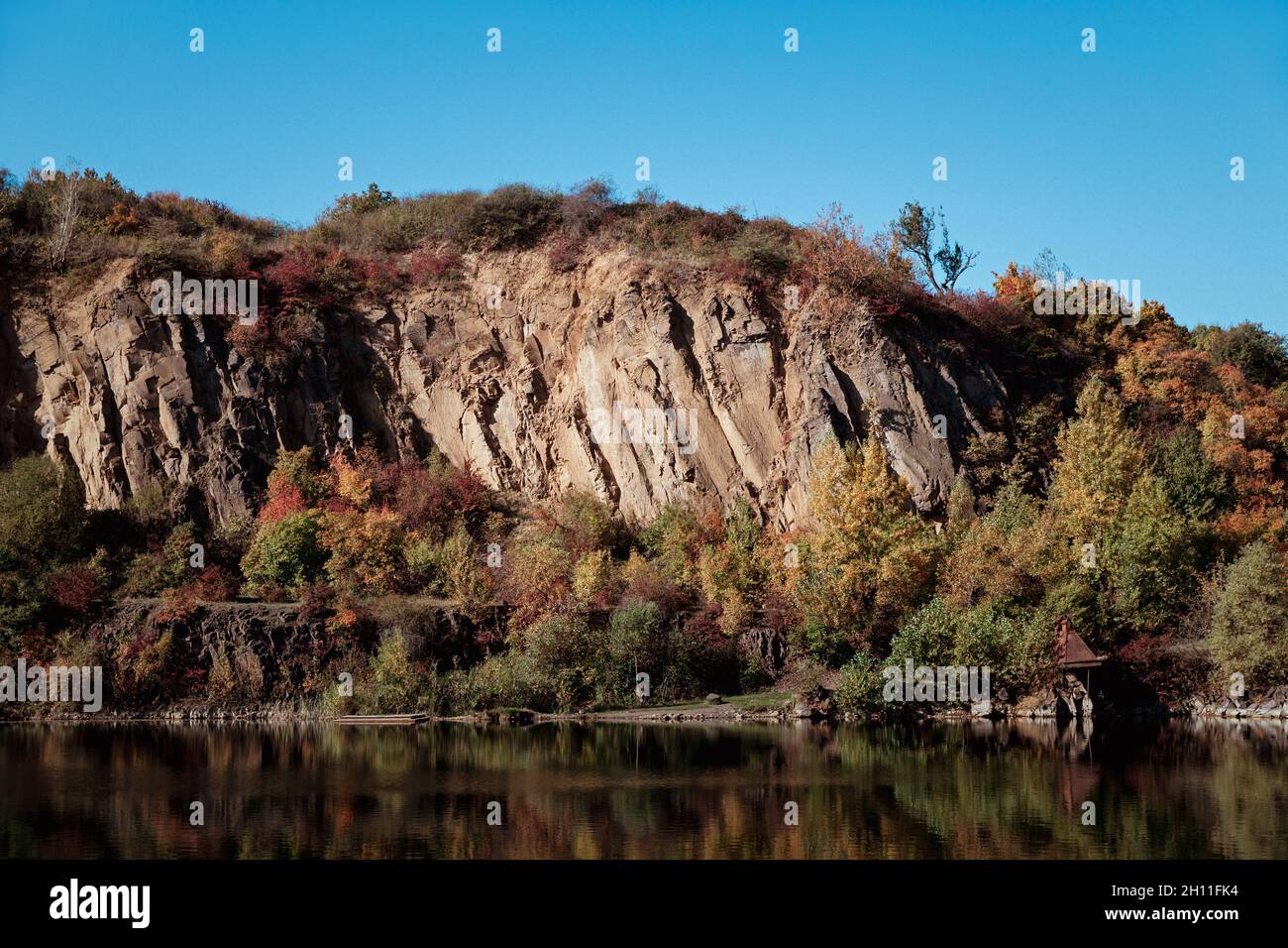 Golden autumn with colourful trees in old flooded quarry. Rocks, lake ...