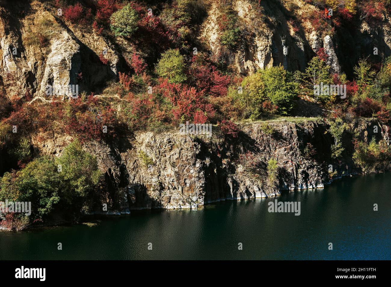 Golden autumn with colourful trees in old flooded quarry. Rocks, lake ...