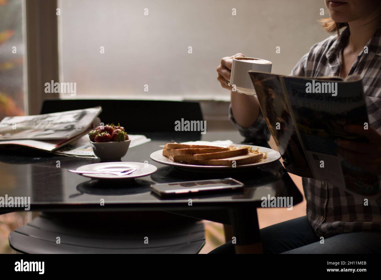 Woman eating breakfast and drinking coffee while reading a magazine ...