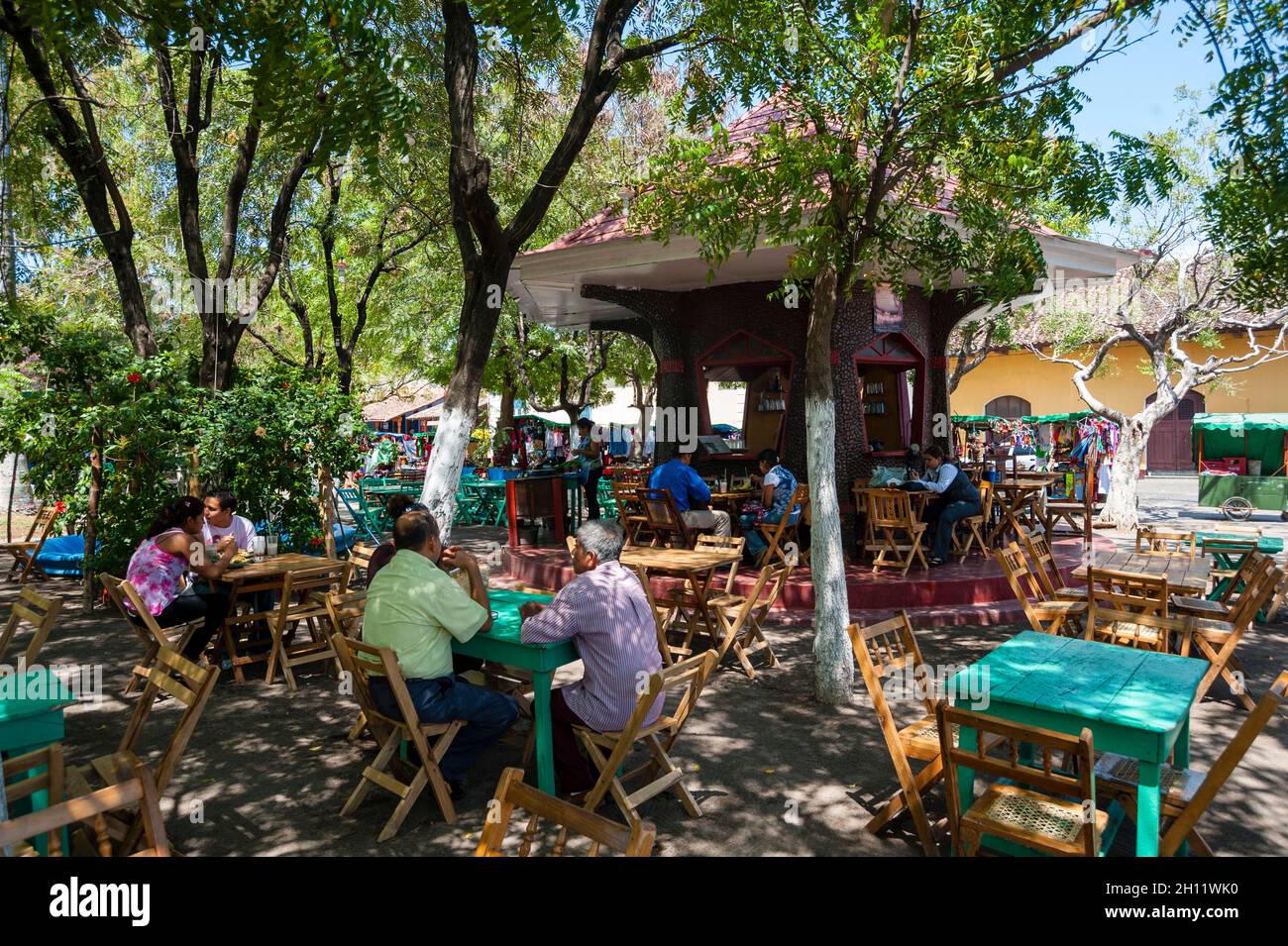 People relaxing in the shade trees in the town's central park. Parque ...