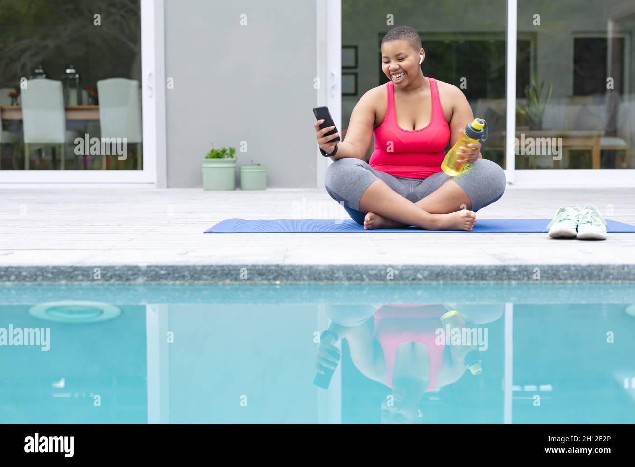 Happy african american plus size woman sitting on mat and using ...