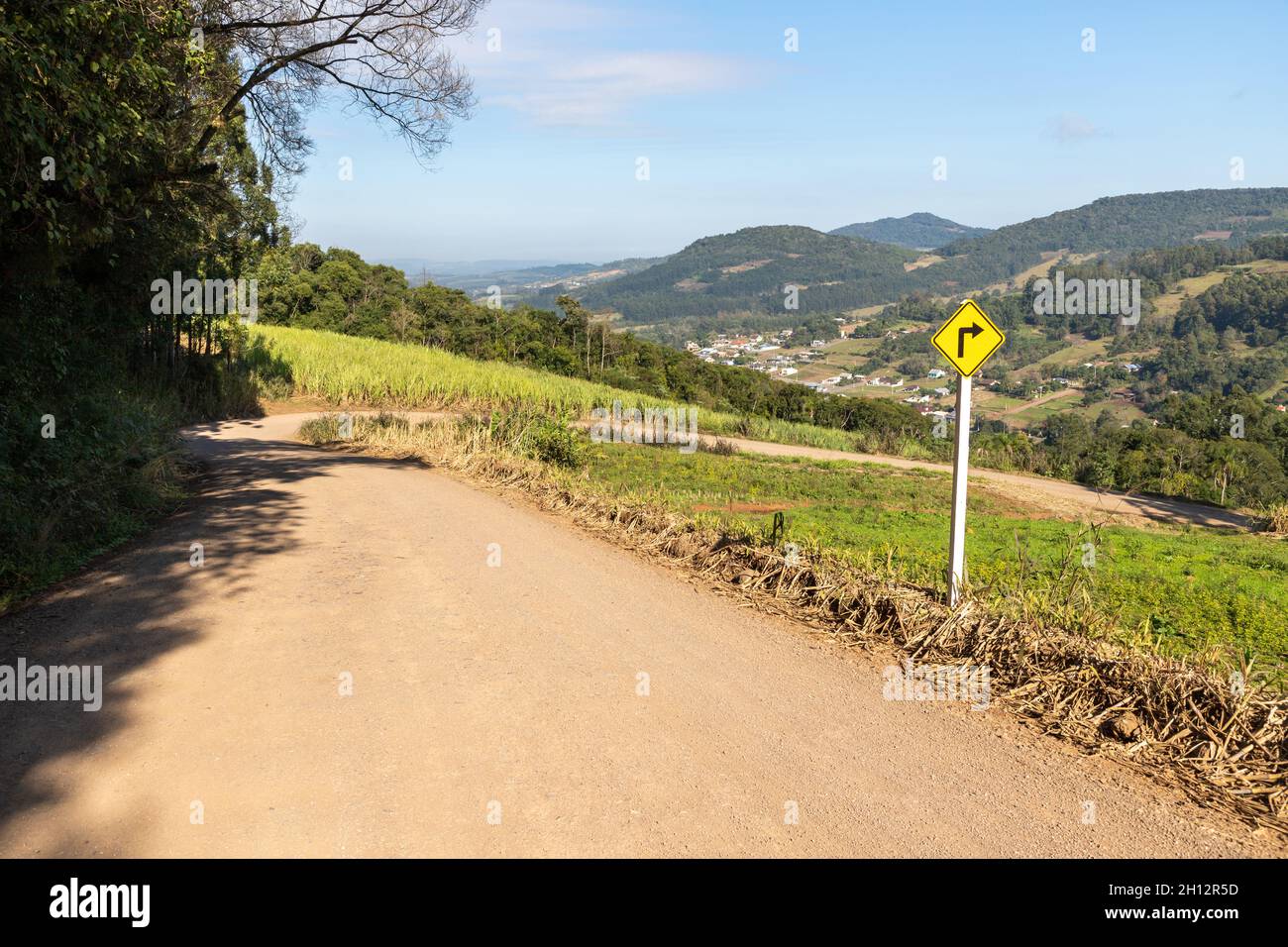 Dirty road with turn right sign, farm fields and village in Sao Jose do ...