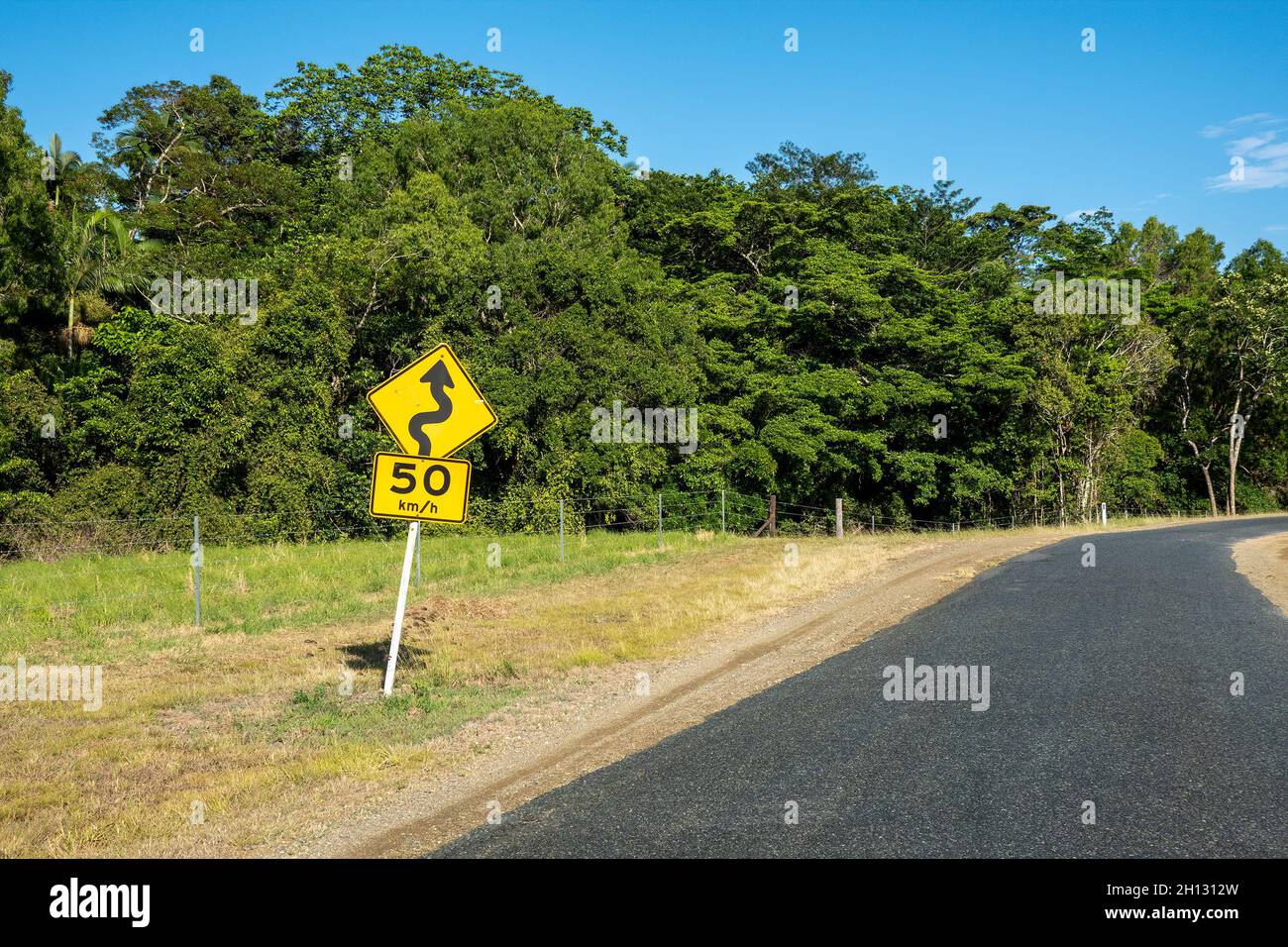 A crooked speed sign on a winding road through bushland indicating the ...