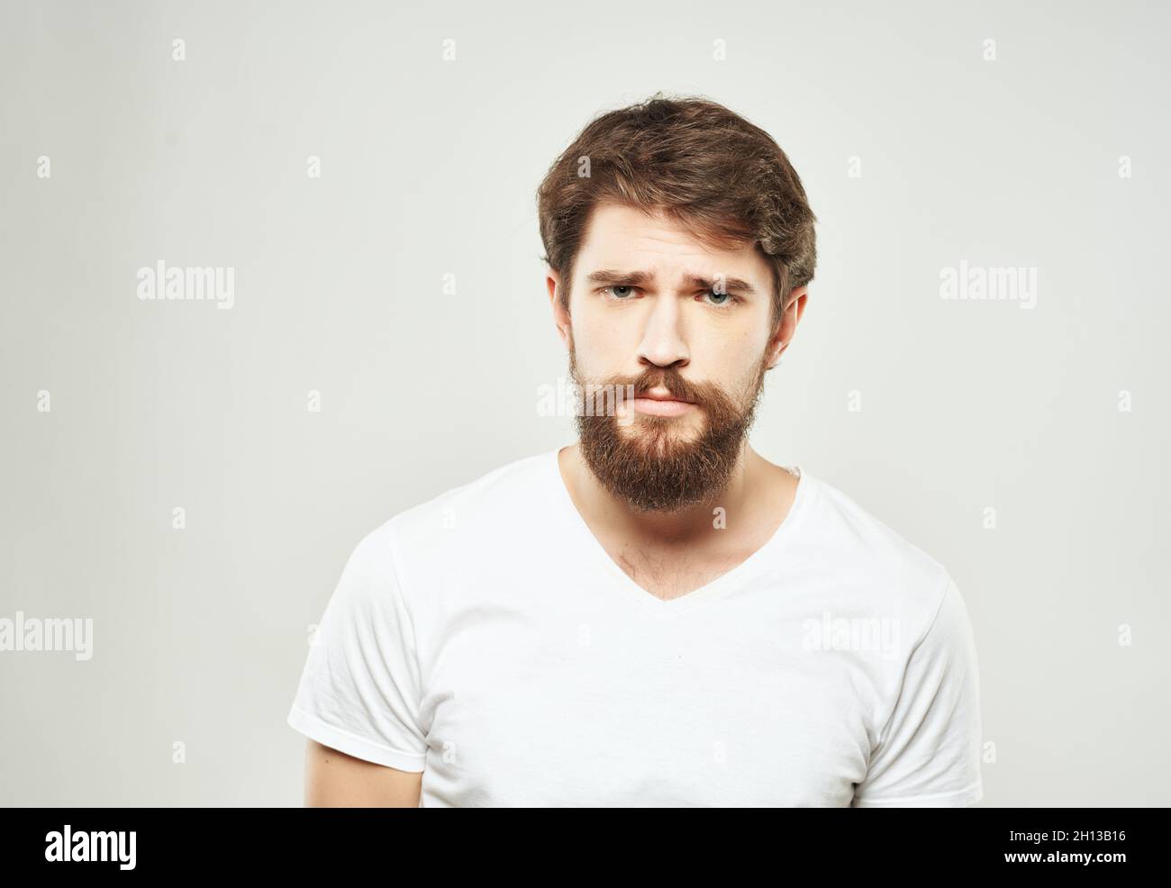 bearded man in a white t-shirt irritated facial expression light ...
