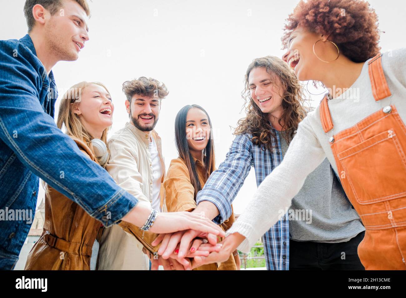Portrait of happy university friends stacking hands together, showing ...