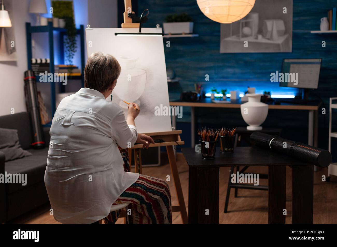 Elder woman drawing vase design from table on canvas while sitting in ...