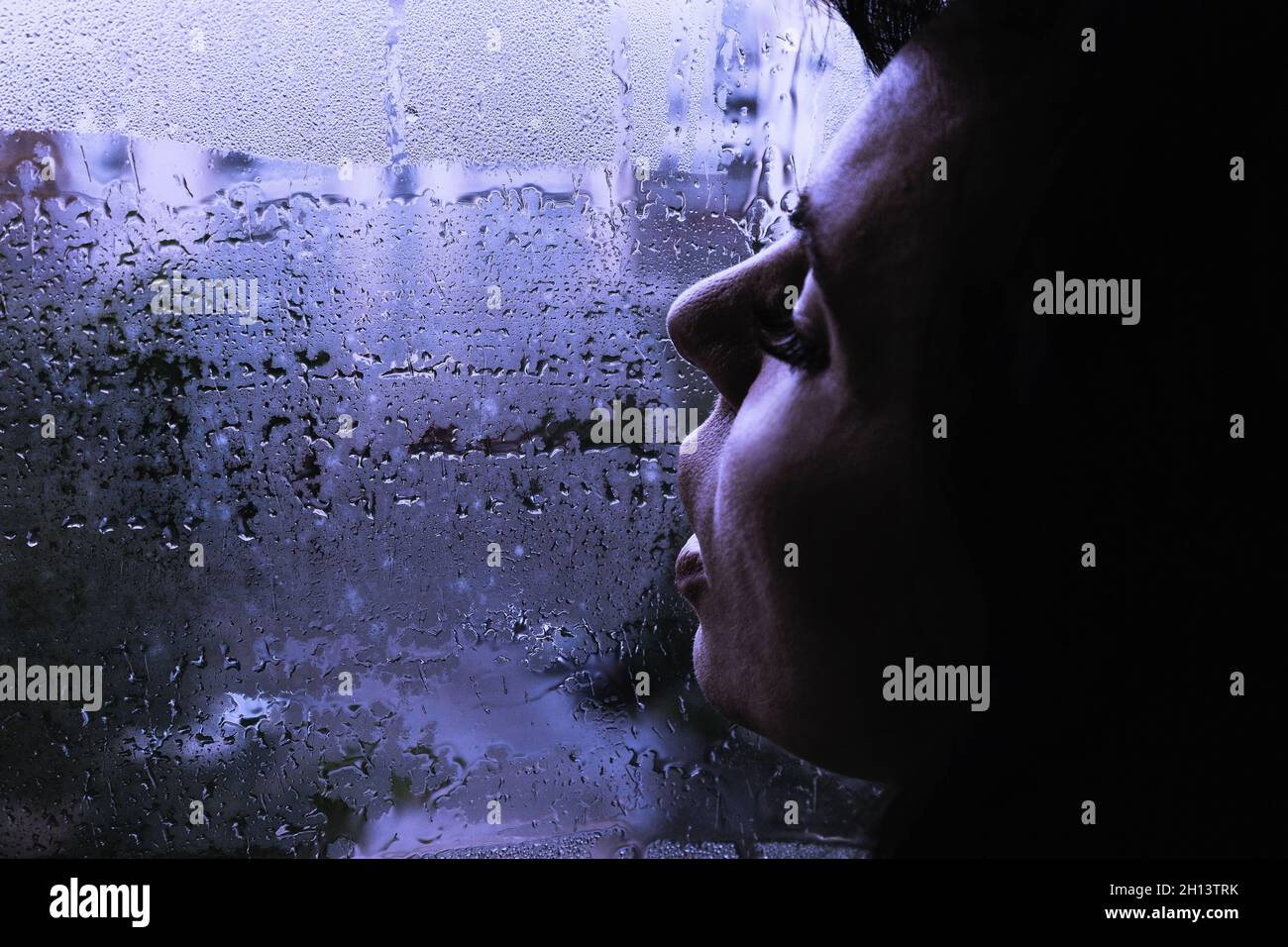 A sad woman blows air with her lips on window fogged from the rain. The ...