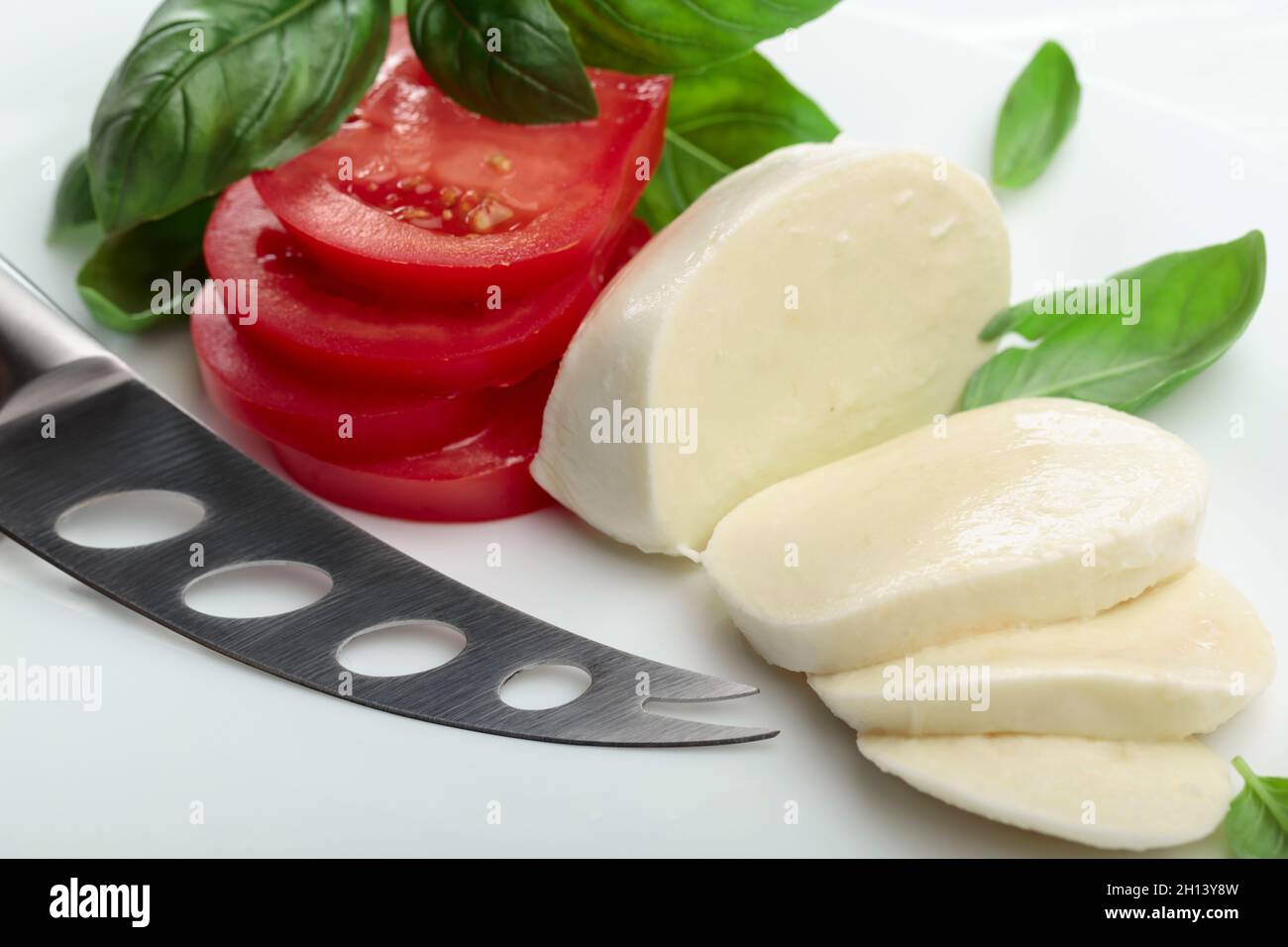 Fresh mozzarella with red tomatoes and green basil on a white plate ...