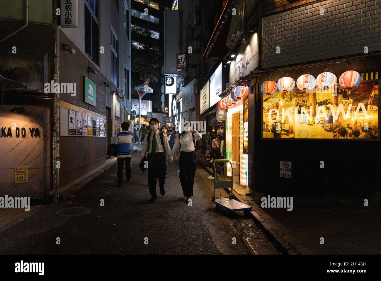 People wearing masks walk through an alley in Shibuya district, Tokyo ...