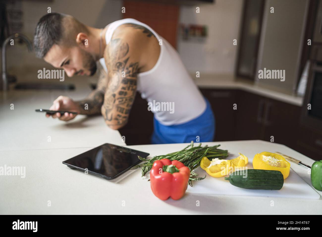 Young fit male using his smartphone while cooking healthy food in the ...