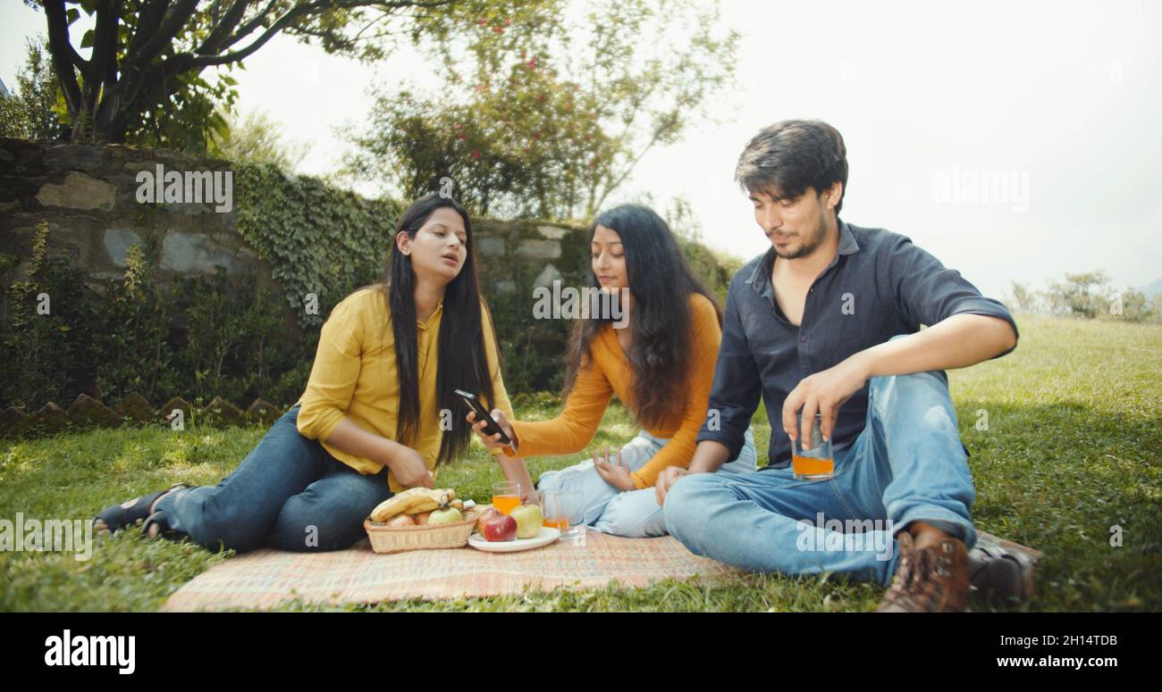 Shot of three young South Asian friends sitting at a picnic blanket ...
