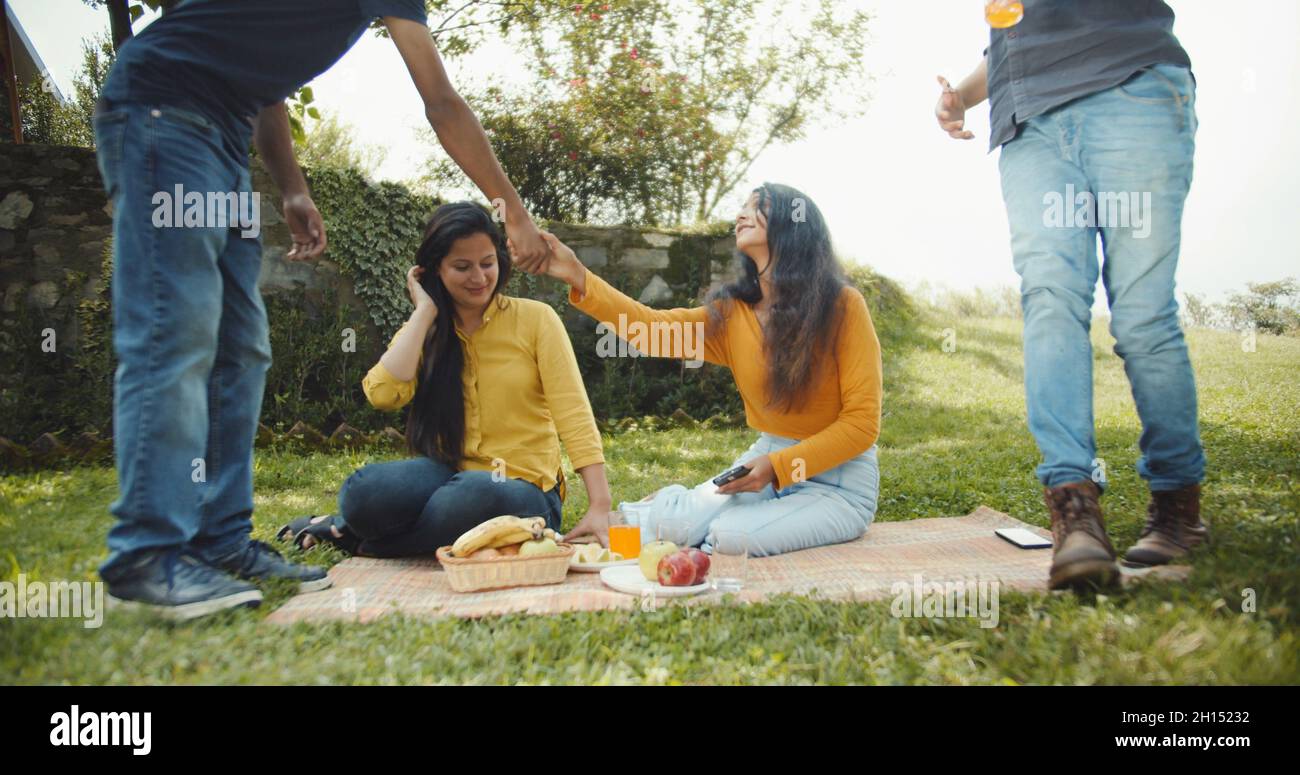 Shot of four young South Asian friends sitting at a picnic blanket with ...