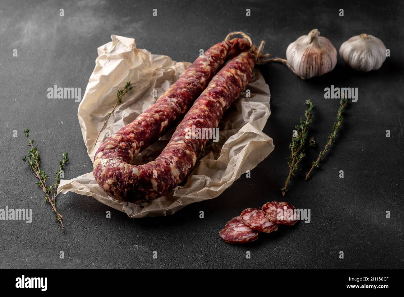 bunch of red dry homemade sausage on a dark background, garlic and ...