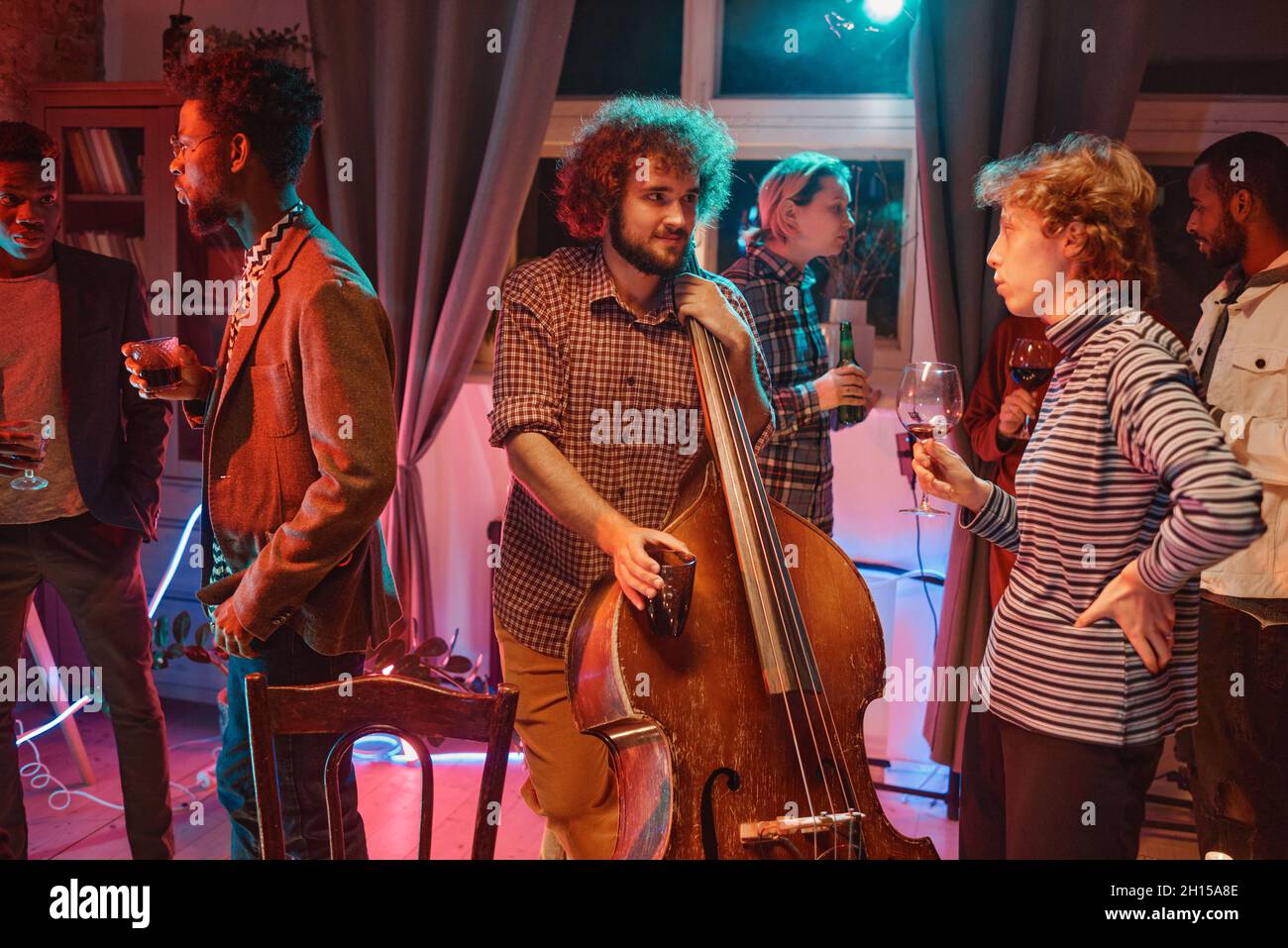 Young musician playing violin at a party while other people talking and ...