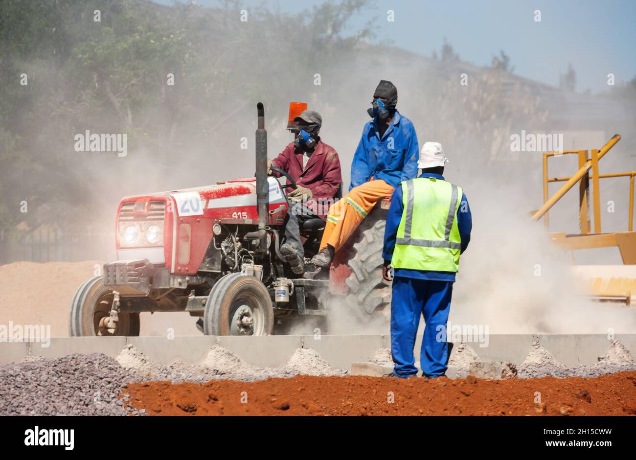 African construction workers riding a tractor on a construction site ...