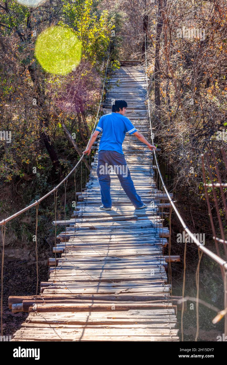 Caucasian young man crossing the shaky wire bridge in the dry African ...