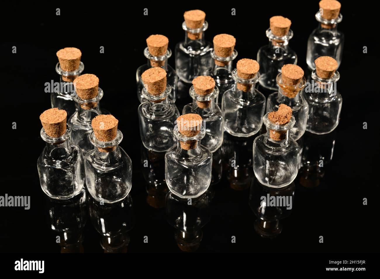 Glass bottles with cork on a black mirror surface with reflections ...