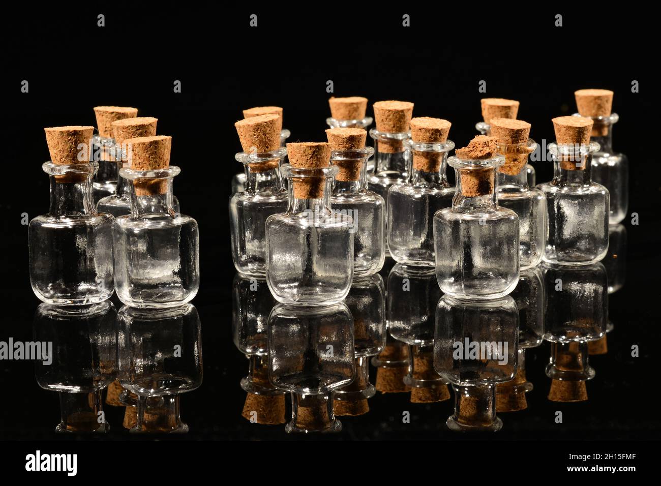 Glass bottles with cork on a black mirror surface with reflections ...