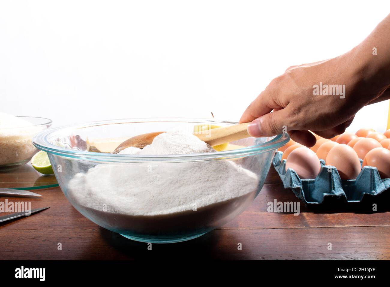 Hand pouring flour into a bowl with a wooden spoon. Using wooden spoon ...